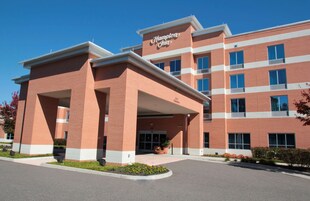 Um hotel Hampton Inn com fachada de tijolos, entrada coberta e estacionamento.