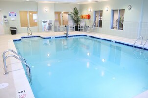 Piscina interior com água azul cristalina, cercada por paredes de azulejos brancos e um vaso de planta.