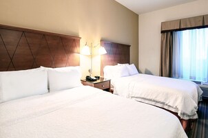 Quarto de hotel com duas camas, uma mesa de cabeceira com abajur e uma janela com cortinas.