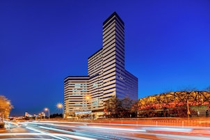 Um hotel com vários andares e design moderno, com uma estrutura de esquina imponente e um edifício curvo grande ao fundo.