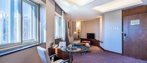 Quarto de hotel com escrivaninha, cadeira, televisão e uma grande janela.