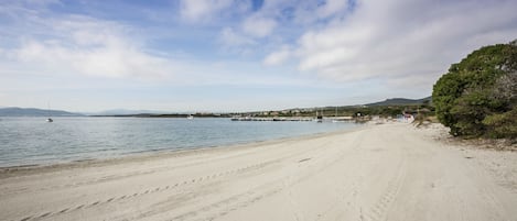 Uma praia com areal, águas calmas e colinas ao longe.