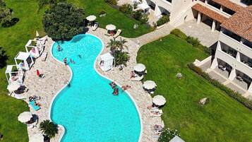 Vista aérea de um resort com uma piscina grande, espreguiçadeiras e um gramado bem cuidado.
