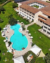 Vista aérea de um resort com uma piscina grande, espreguiçadeiras e um gramado bem cuidado.