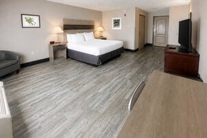 Quarto de hotel com cama, mesas de cabeceira, escrivaninha, cadeira e televisão.