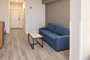 Um corredor com um sofá azul, uma mesa pequena e uma porta com interruptor de luz.