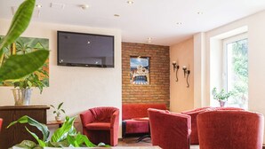 Sala de estar com poltronas vermelhas estofadas, uma TV de tela plana fixada na parede, uma parede de tijolos decorativa e uma janela que permite entrada de luz natural.