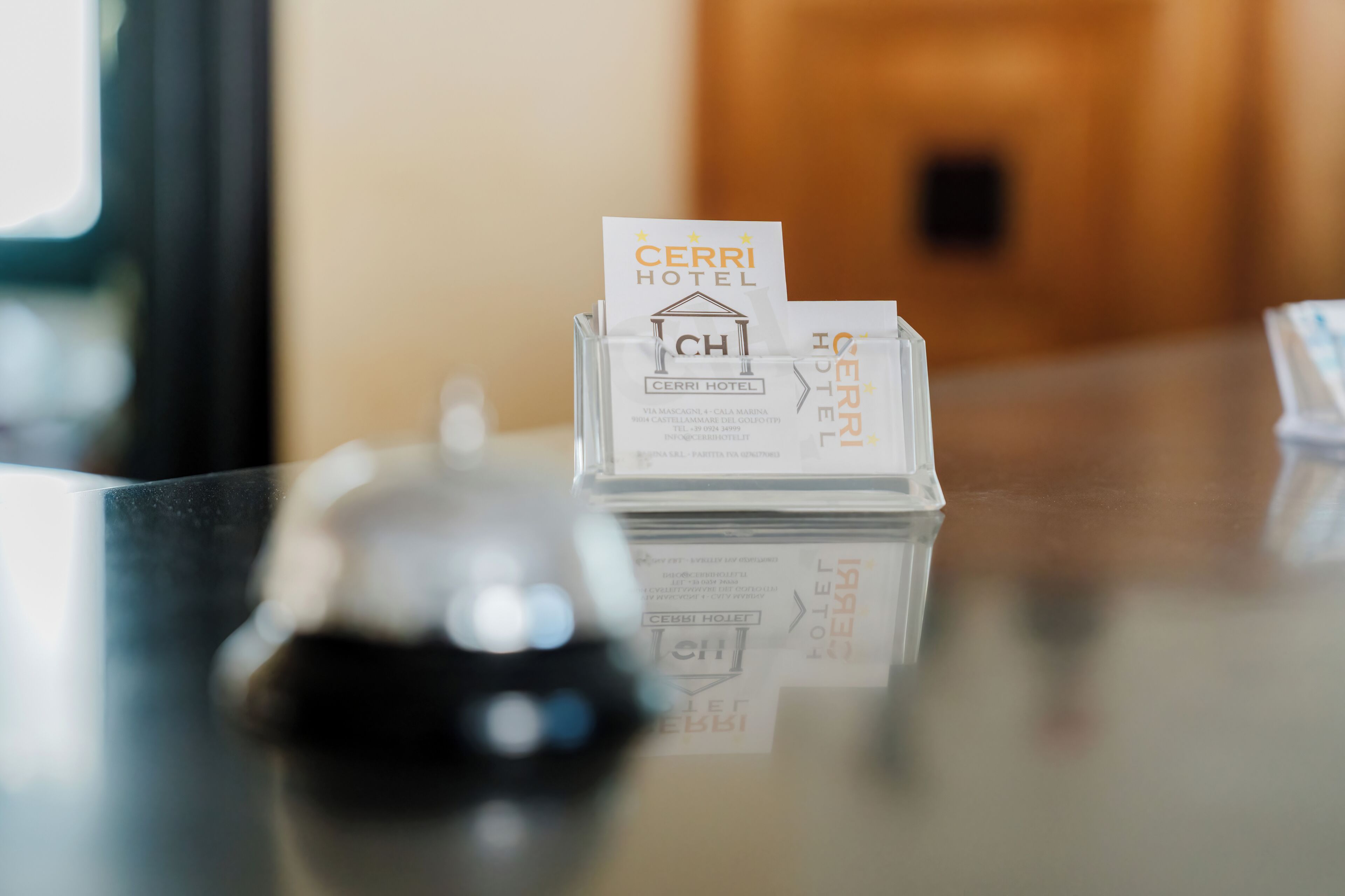 Bancada de recepção de hotel com uma vitrine de vidro contendo cartões de visita e um sino.