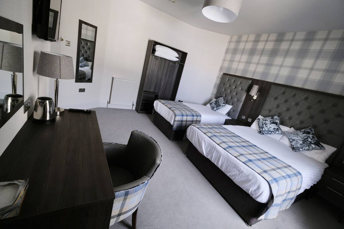Quarto de hotel com duas camas, uma escrivaninha, uma cadeira, um espelho e uma televisão.