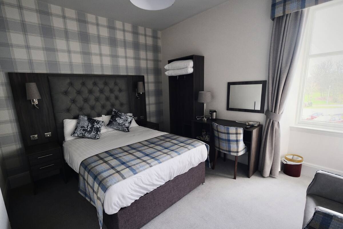 Quarto de hotel bem arrumado, com uma cama grande, uma escrivaninha, uma cadeira e um guarda-roupa.