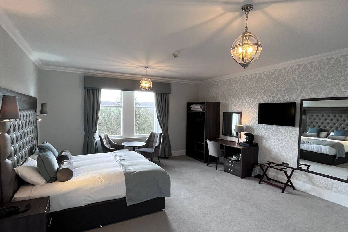 Quarto de hotel moderno com uma cama grande, uma mesa, uma cadeira e uma televisão.