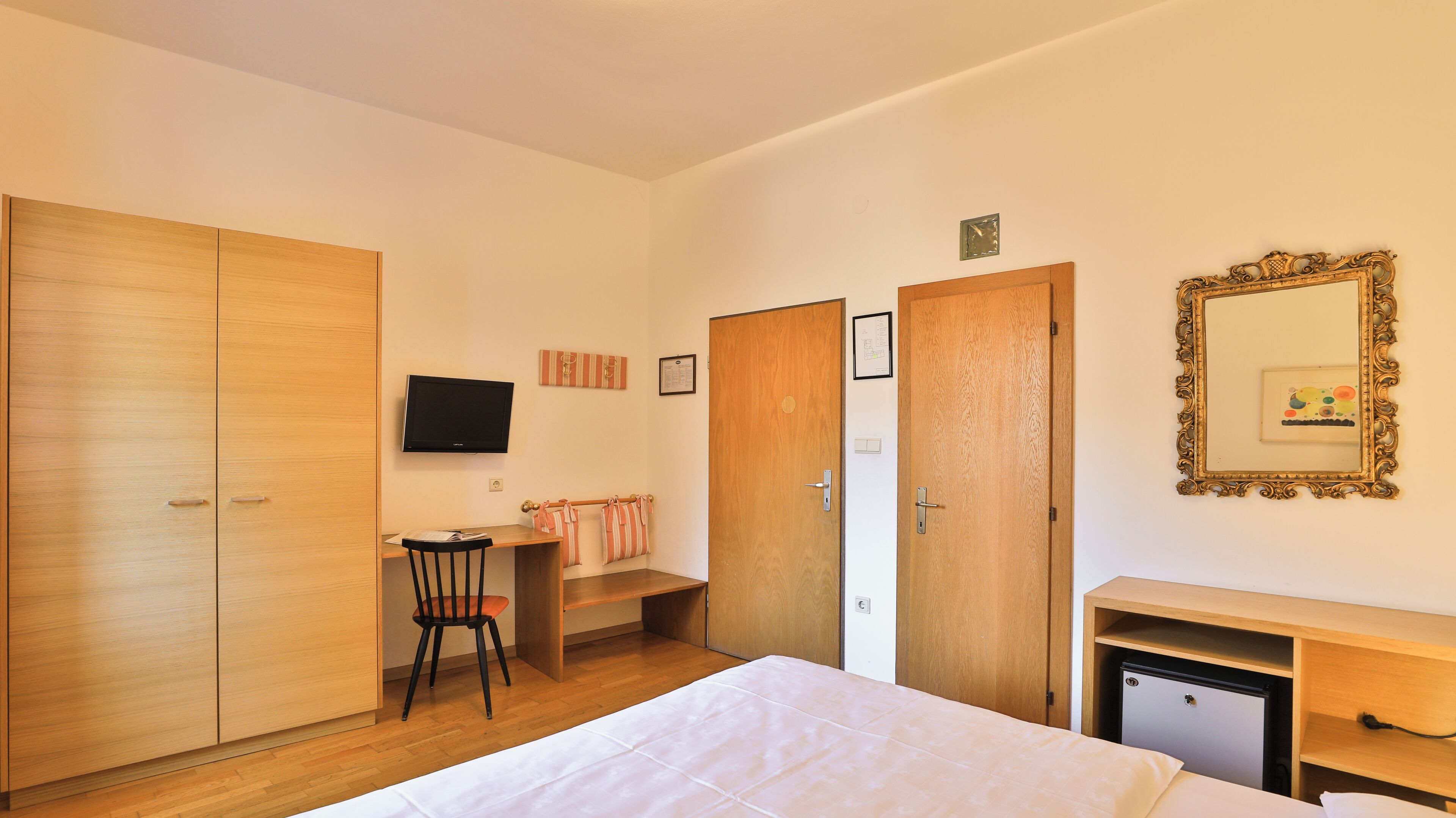 Quarto com cama, escrivaninha, cadeira, televisão e guarda-roupa.