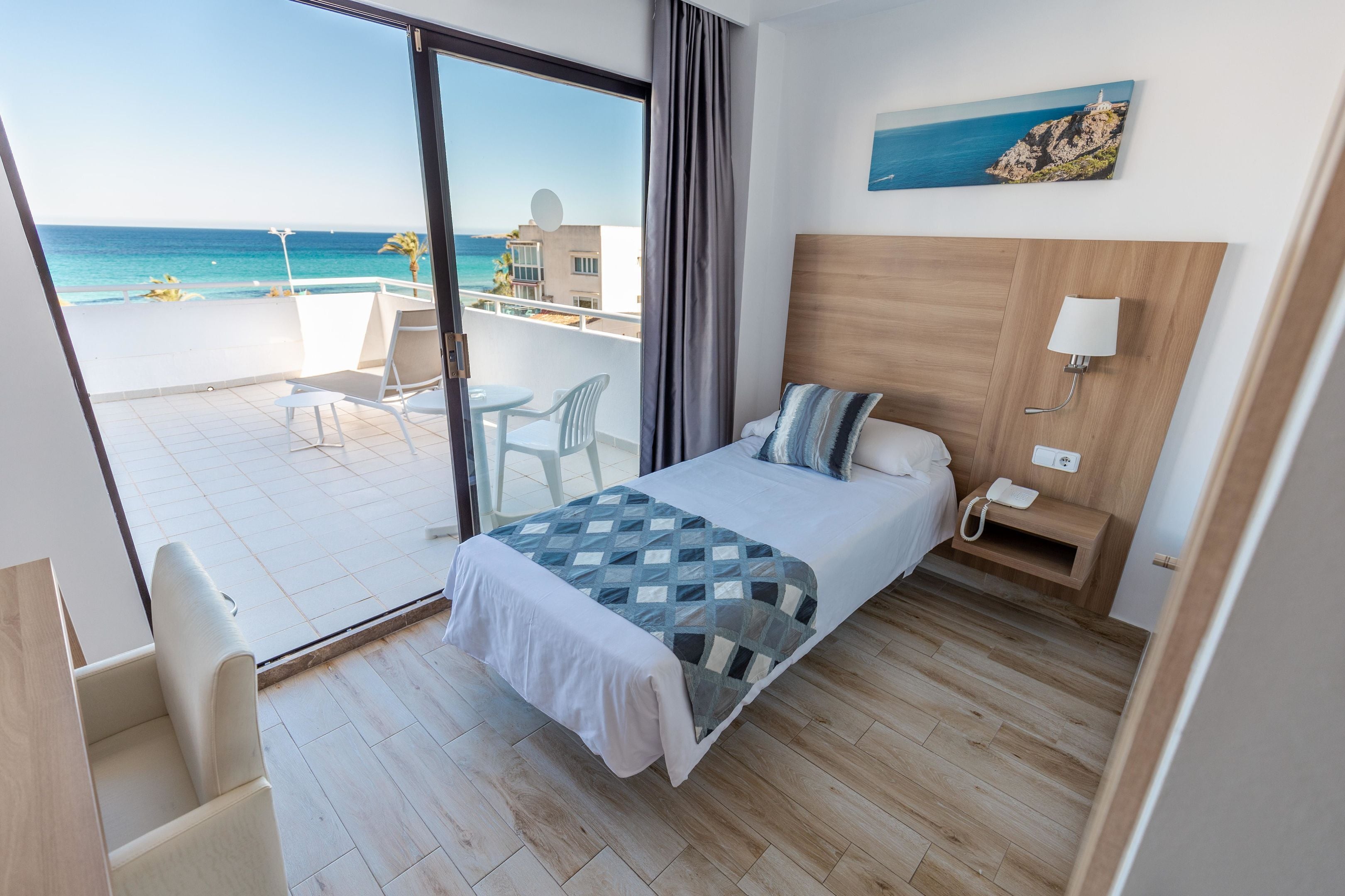Quarto de hotel com cama, mesa de cabeceira, abajur, telefone e vista para o mar.