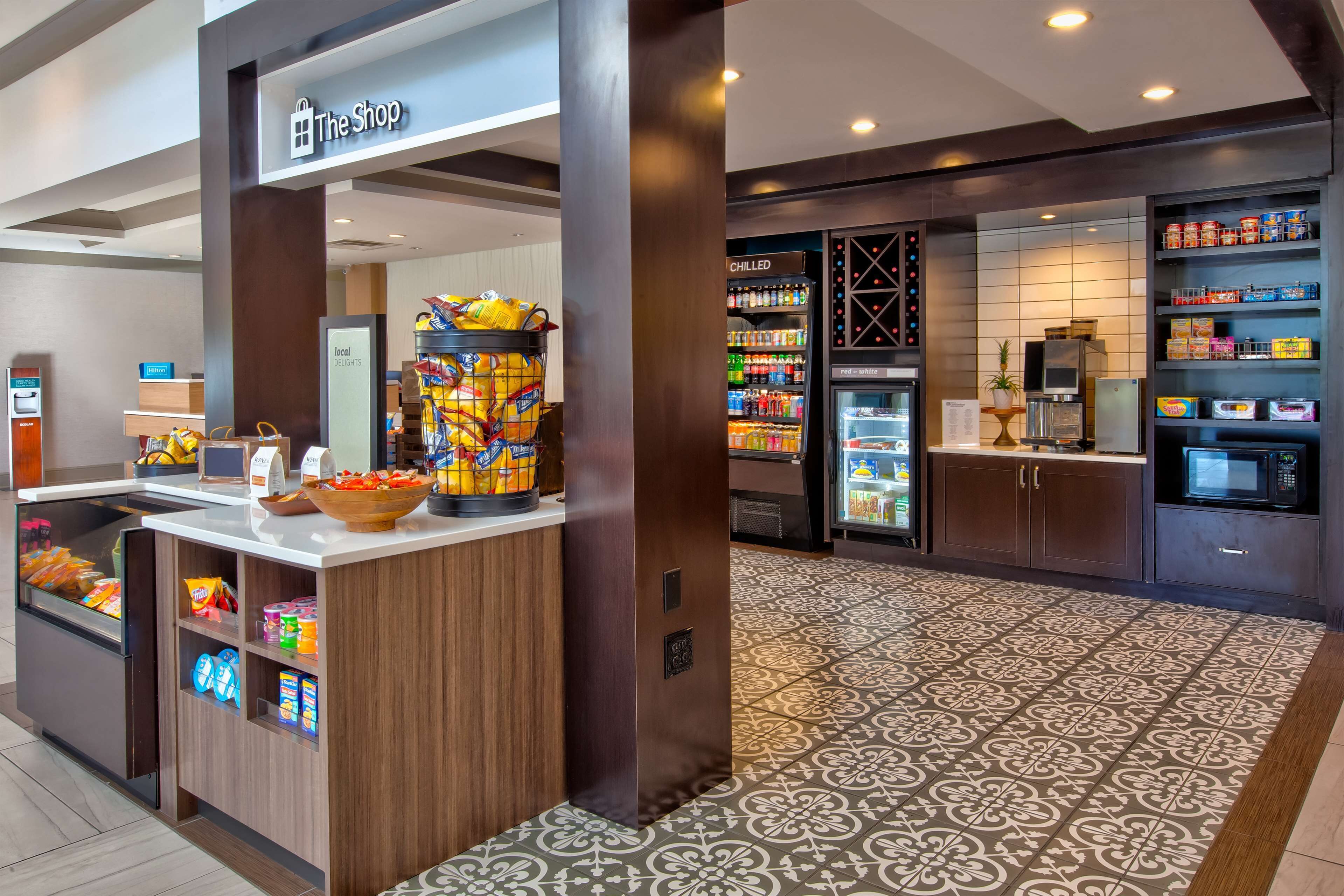 Uma área de serviço de alimentação em hotel, com balcão de autoatendimento, bebidas refrigeradas e micro-ondas.