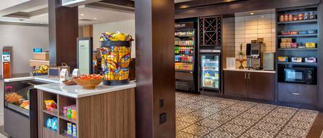 Uma área de serviço de alimentação em hotel, com balcão de autoatendimento, bebidas refrigeradas e micro-ondas.
