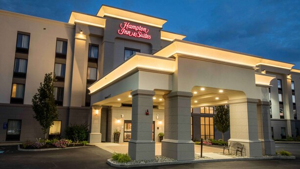 Um hotel Hampton Inn & Suites com fachada moderna, colunas grandes e entrada bem iluminada.