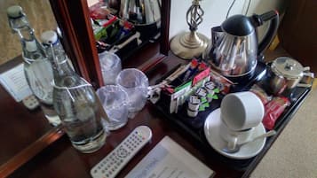 Minibar num quarto de hotel, com comando, copos, um tabuleiro com chávenas e snacks, e uma lâmpada.