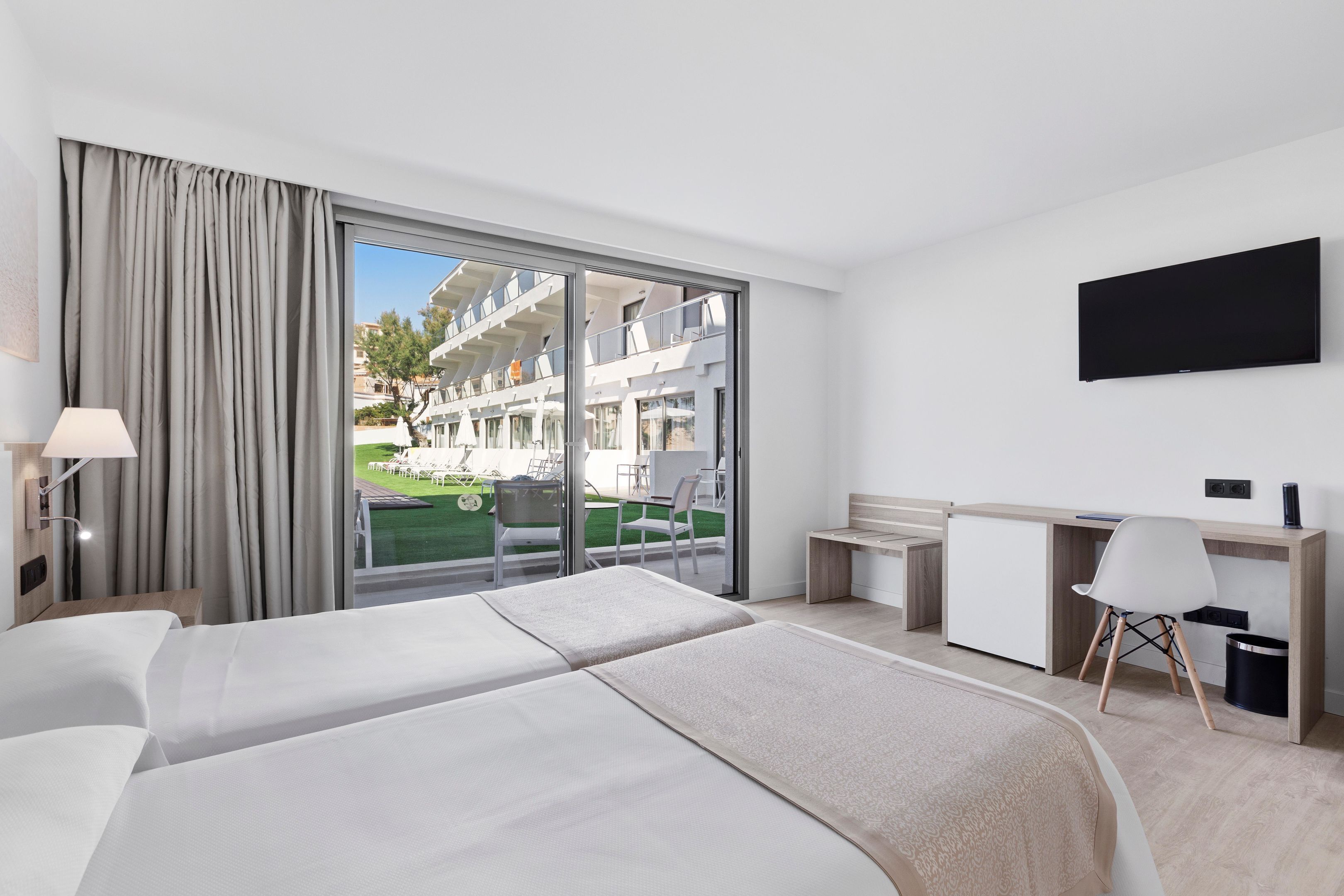 Quarto de hotel com duas camas, uma escrivaninha, uma cadeira, uma televisão e vista para a área externa.