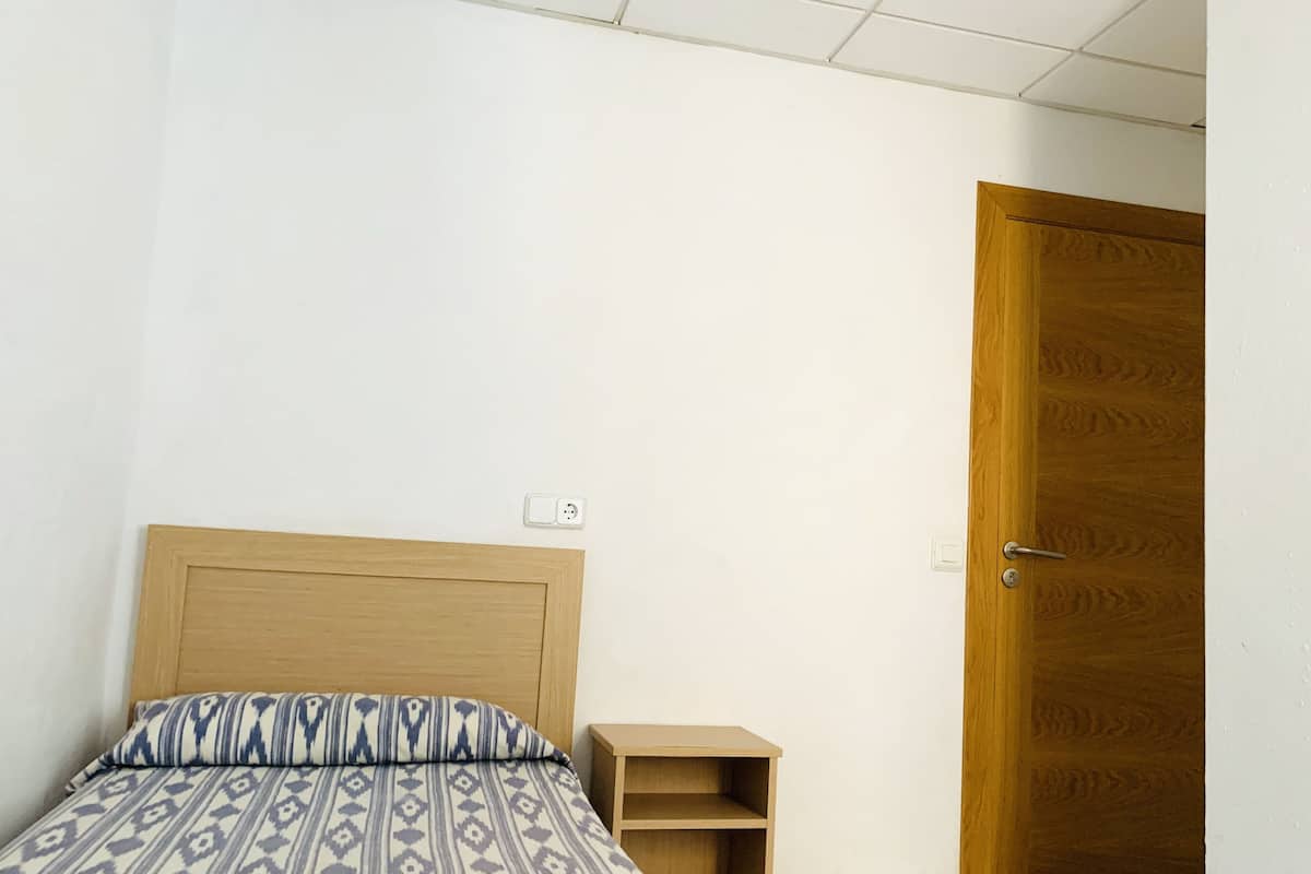 Quarto com cama, cabeceira de madeira, mesa de cabeceira, guarda-roupa e tomada na parede.