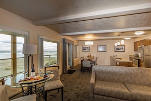 Quarto de hotel com área de refeições, cozinha e grandes janelas com vista para a praia.