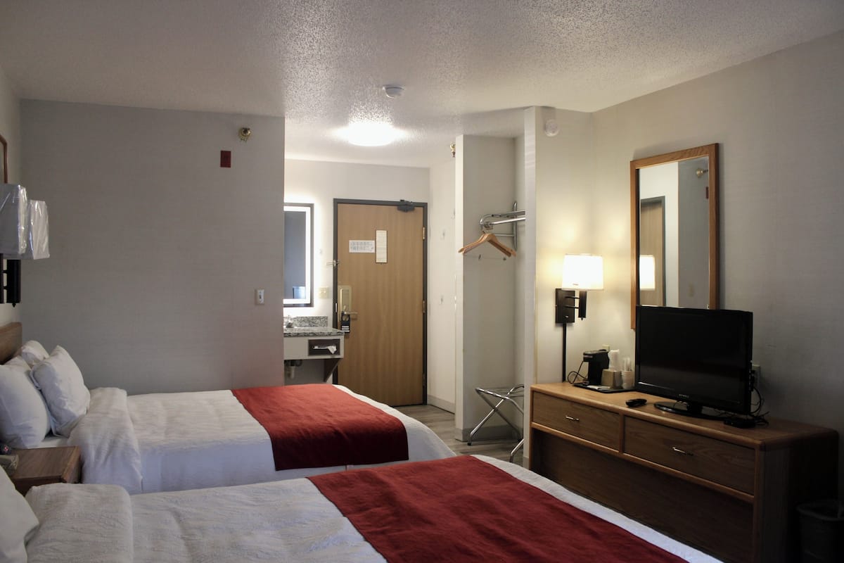 Quarto de hotel com duas camas, televisão, escrivaninha com candeeiro e espelho na parede.