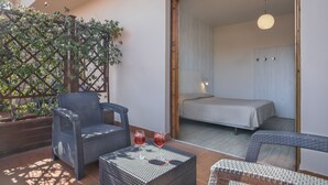 Varanda com mobiliário de vime, dois copos de vinho tinto e uma cama no quarto adjacente.