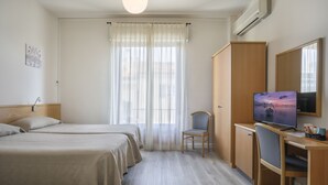 Quarto de hotel com duas camas, uma escrivaninha com computador, uma cadeira e uma televisão.