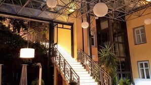 Um lobby de hotel moderno com teto de vidro, escadaria e áreas de estar confortáveis.