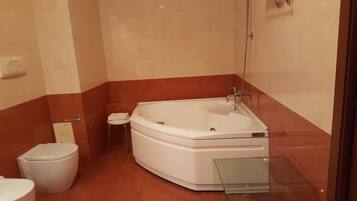 Casa de banho com banheira branca, sanita e cabine de chuveiro em vidro.