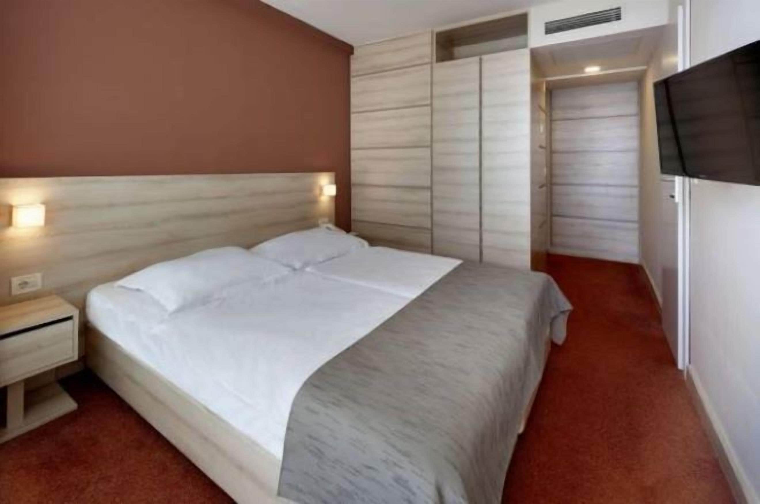 Quarto de hotel com cama, mesas de cabeceira, guarda-roupa e televisão.