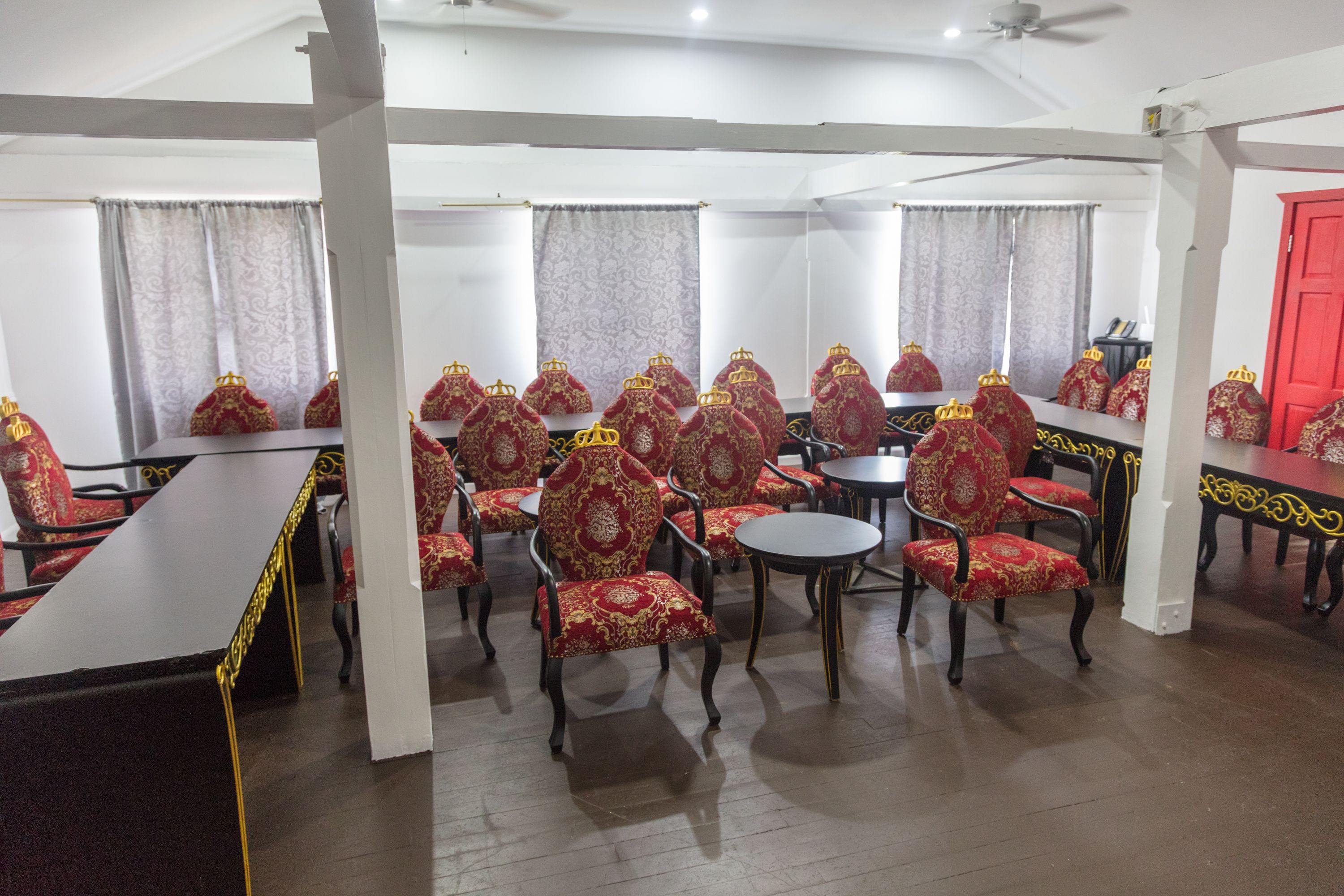 Uma sala de conferências com mesas e cadeiras, paredes brancas e uma porta vermelha.
