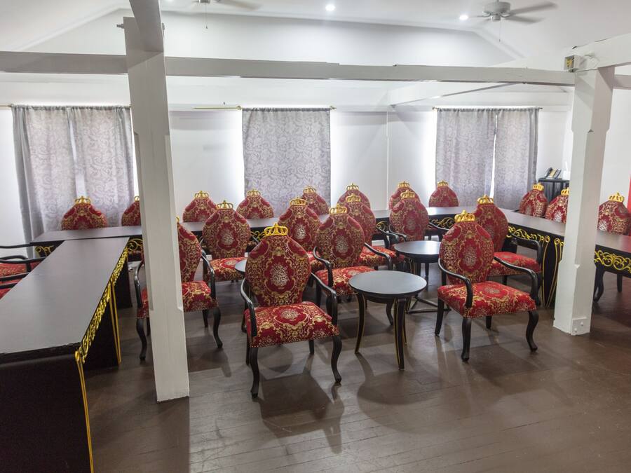 Uma sala de conferências com mesas e cadeiras, paredes brancas e uma porta vermelha.