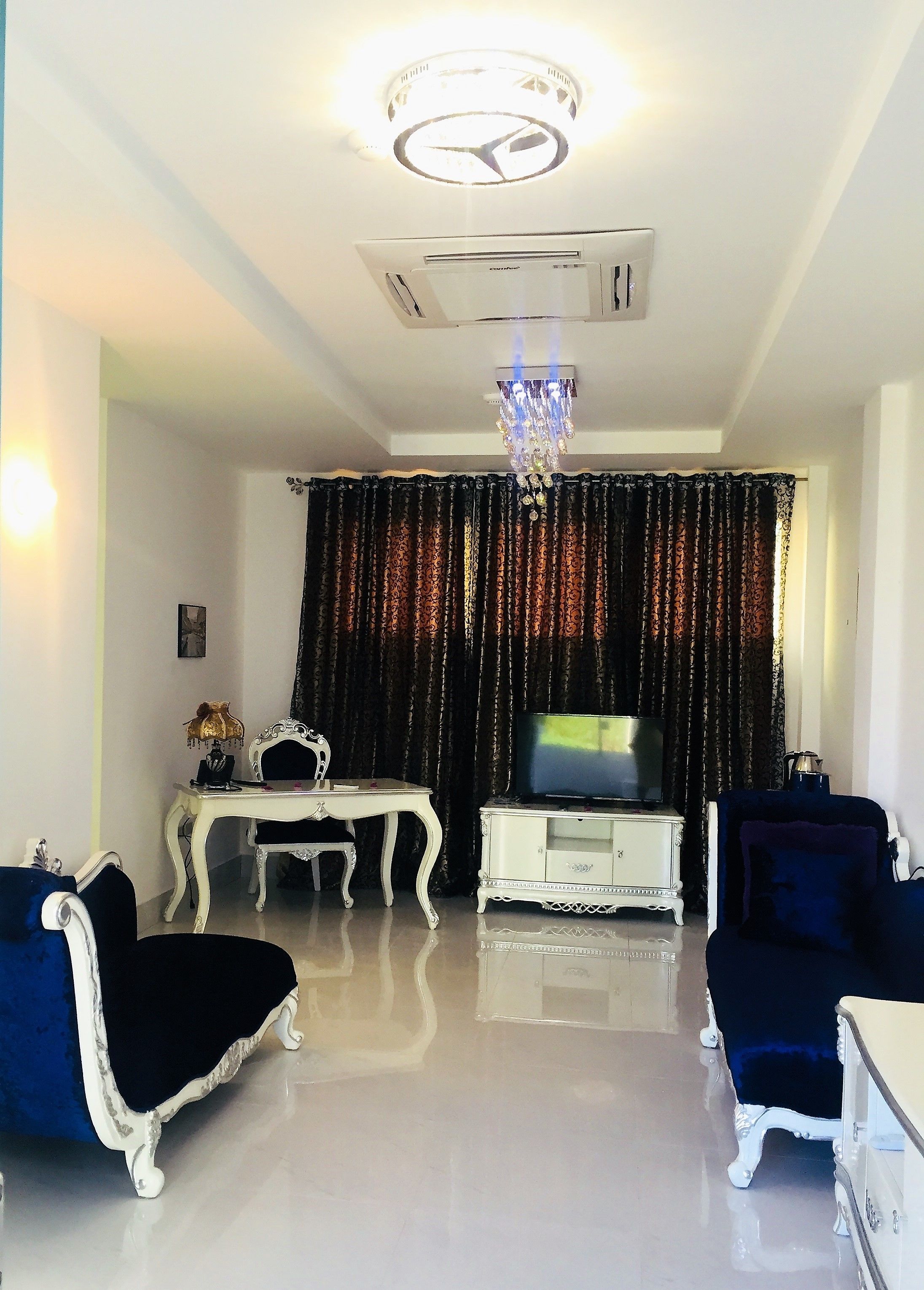 Uma sala de estar com TV, um lustre e um espaço de jantar com mesa e cadeiras.