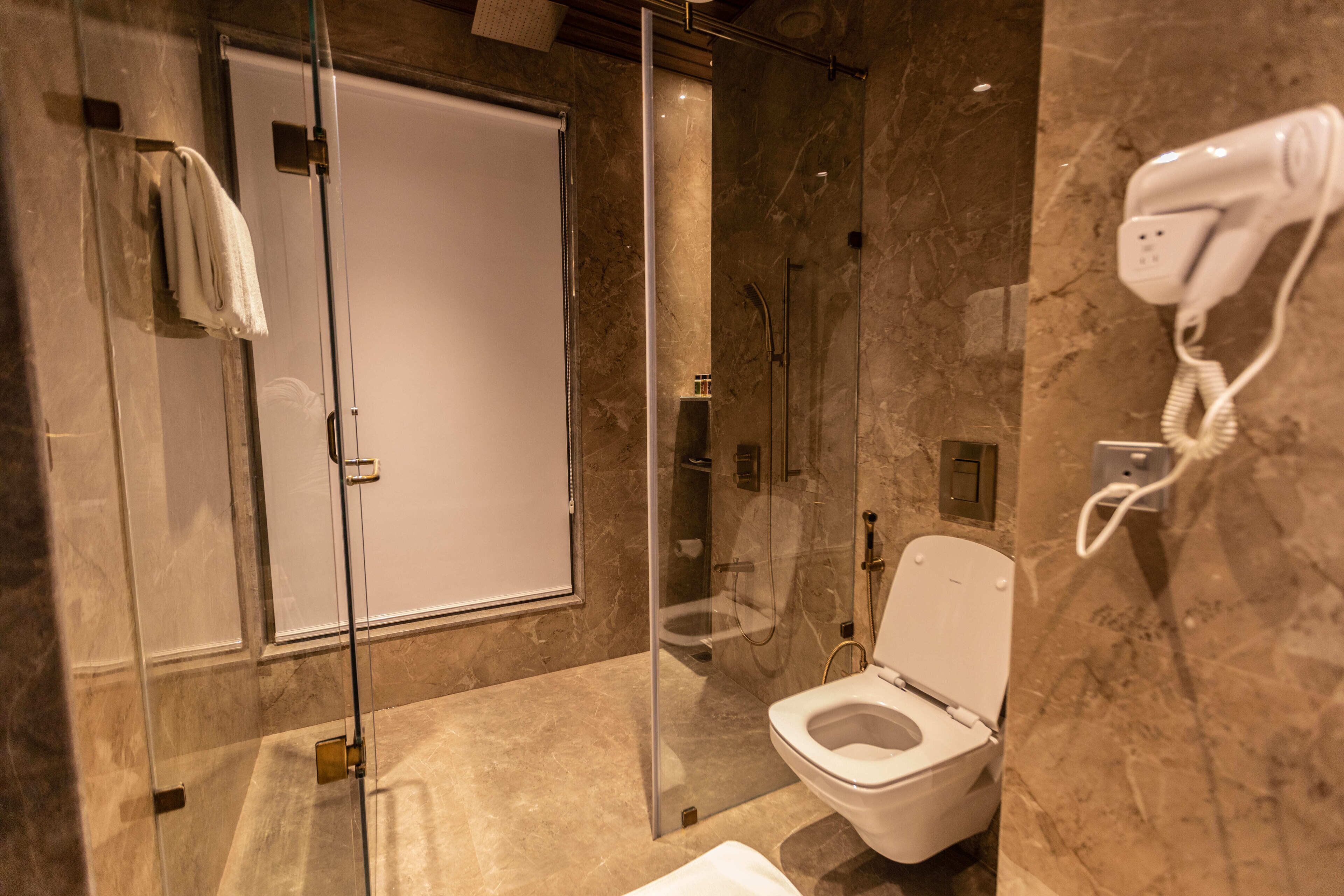 Uma casa de banho moderna com chuveiro em cabine de vidro, sanita branca e secador de cabelo fixado na parede.