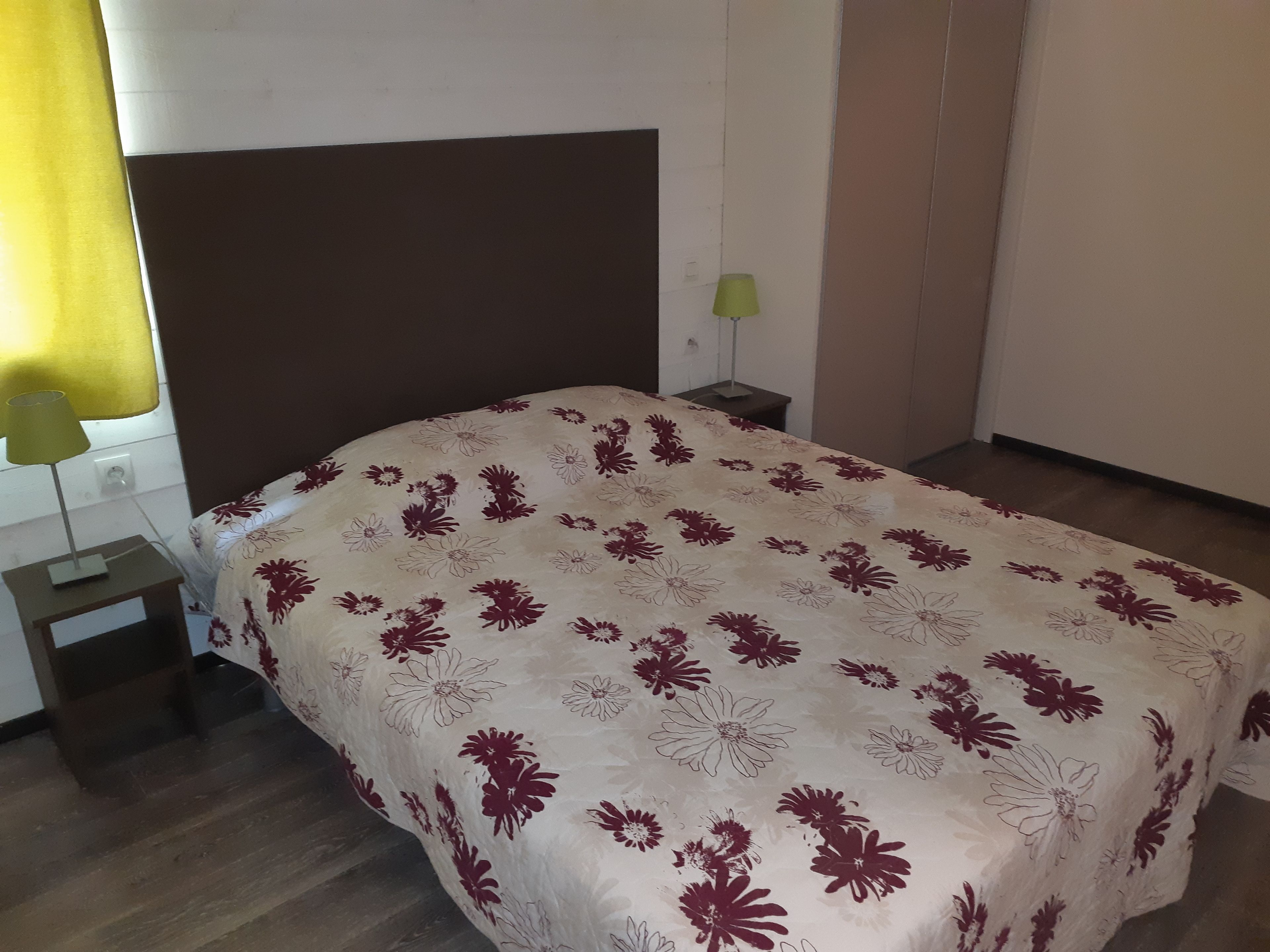 Quarto com cama, mesa de cabeceira, abajur e janela com cortina.
