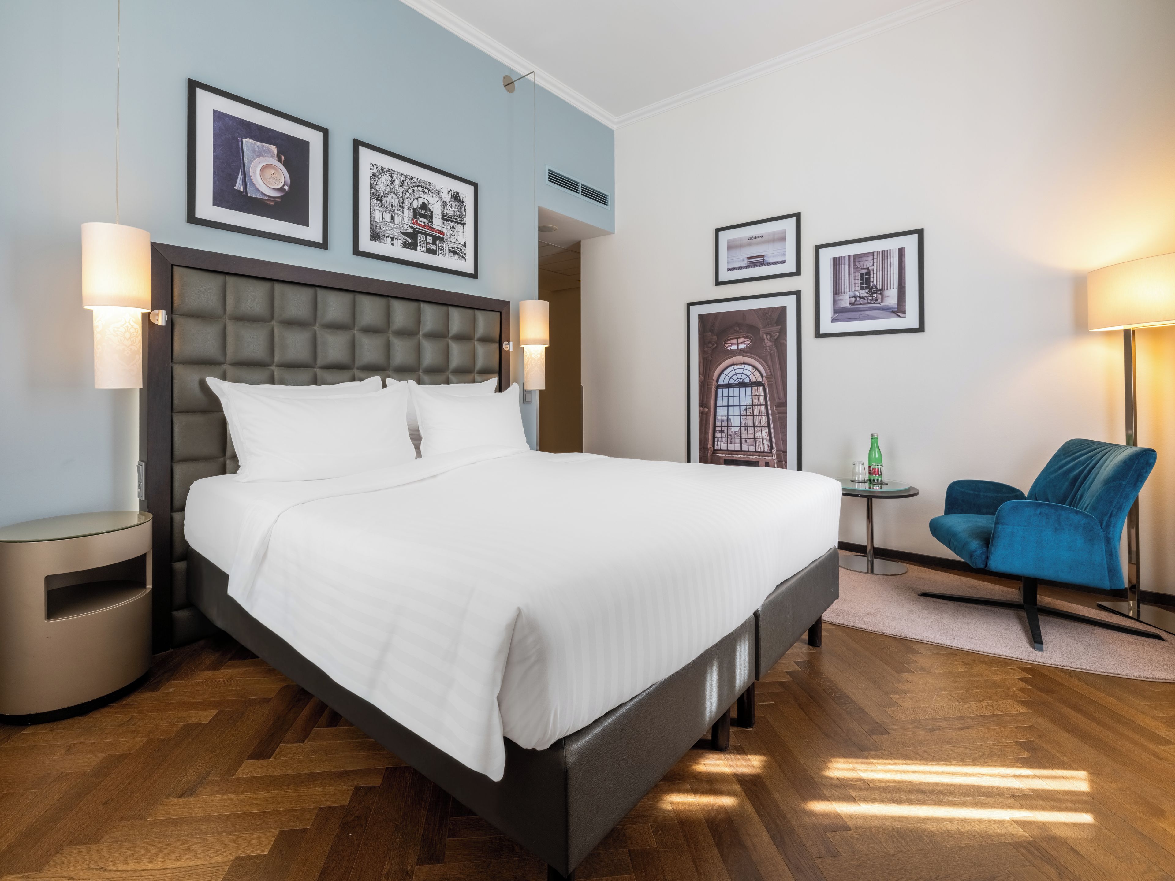 Quarto de hotel com uma cama grande, uma cadeira, uma mesa pequena e obras de arte na parede.
