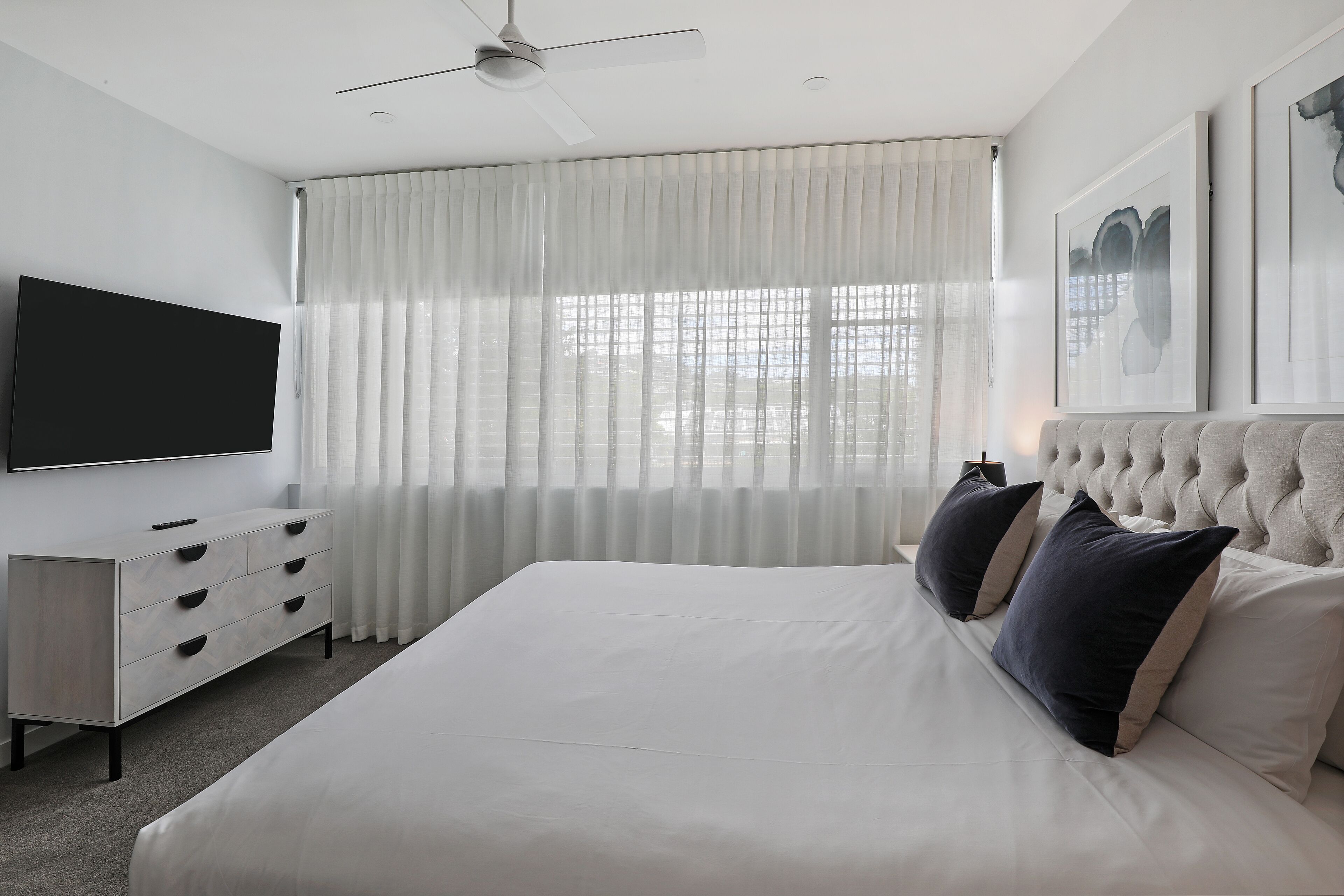 Quarto moderno com cama grande, televisão de tela plana, cômoda e ventilador de teto.