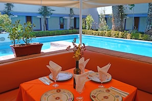 Mesa posta para refeição, com vista para uma piscina e um edifício ao fundo.