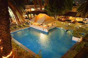 Área de piscina com espaço de estar coberto, espreguiçadeiras e guarda-sóis.