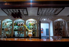 Uma área de bar com prateleiras cheias de garrafas de bebidas, um copo com canudo amarelo e um espelho refletindo o balcão.