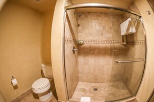 Chuveiro com porta de vidro, vaso sanitário e porta-toalhas.