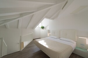 Um quarto moderno com uma cama grande, paredes brancas e teto inclinado.