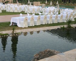 Montagem formal para um evento ao ar livre, com fileiras de mesas e cadeiras, uma piscina e um caminho de pedra.
