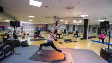 Ginásio com vários tapetes de exercício, equipamentos de yoga e um espelho grande.