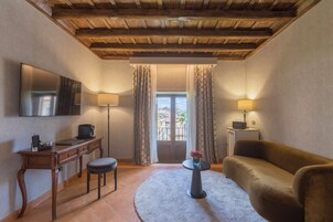 Quarto com teto de madeira, uma escrivaninha com cadeira, um sofá, um tapete redondo e uma TV fixada na parede.
