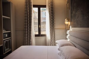 Quarto de hotel com cama, guarda-roupa, cofre e janela com cortinas.