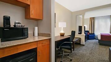 Quarto de hotel com cozinha compacta, escrivaninha, cadeira, cama e televisão.