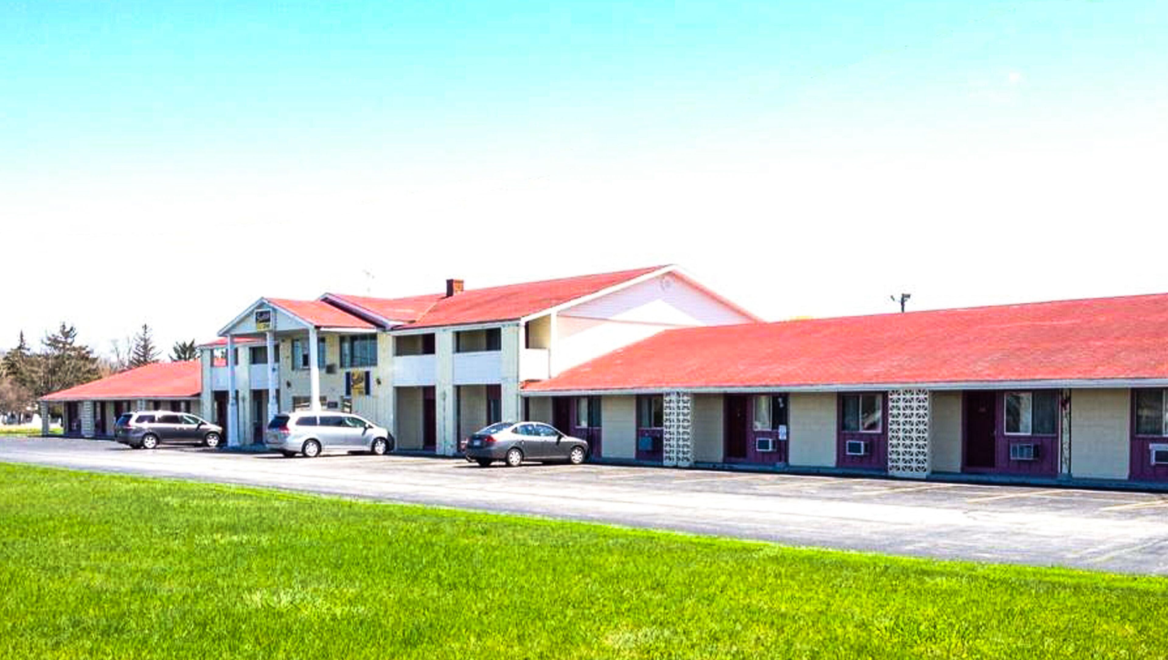 Um motel com telhado vermelho e várias divisões. Há carros estacionados na frente.