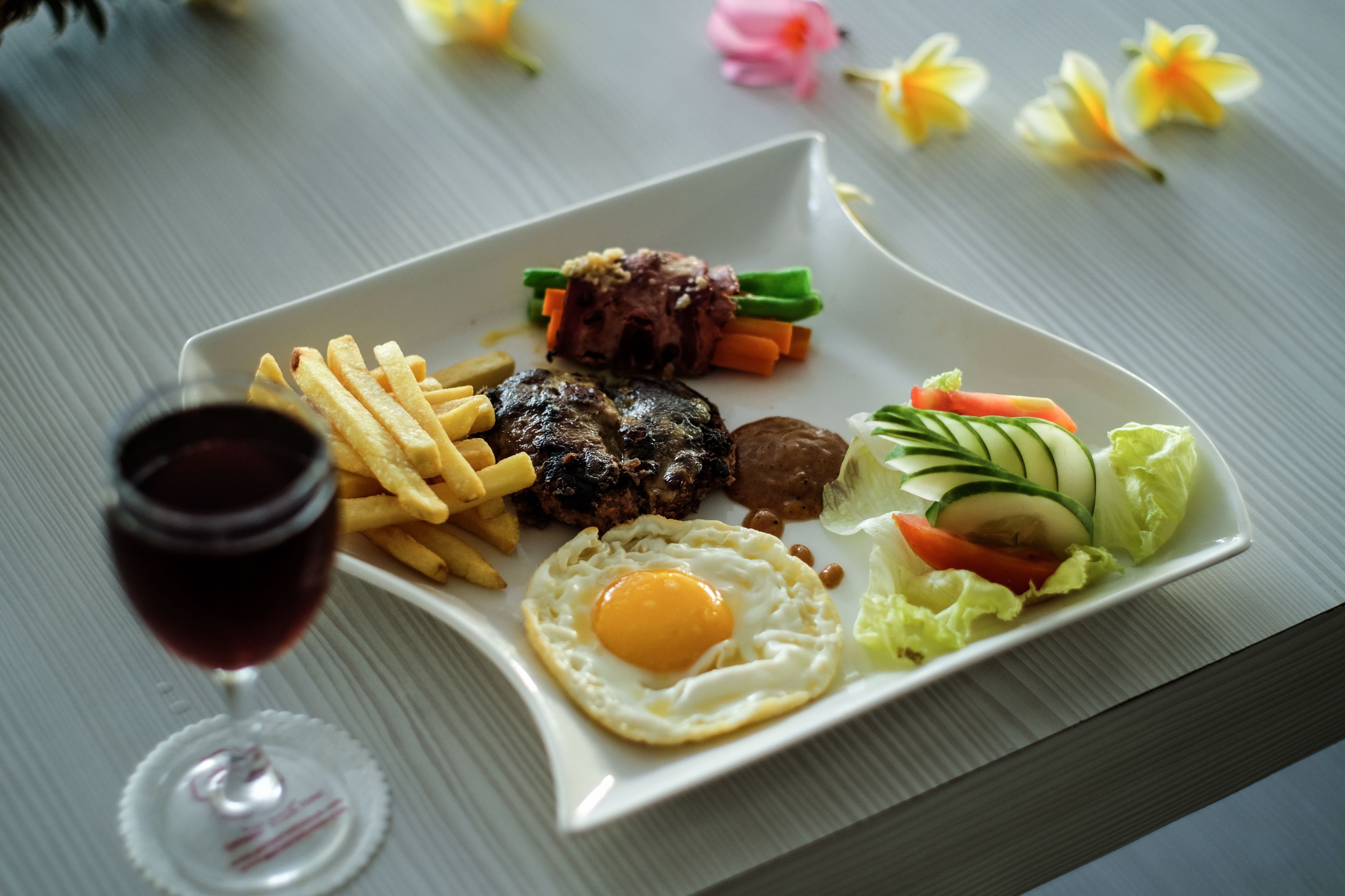 Prato quadrado com bife, batatas fritas, ovo frito e legumes.