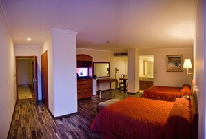 Quarto de hotel com duas camas, uma mesa de trabalho com cadeira, televisão e banheiro.